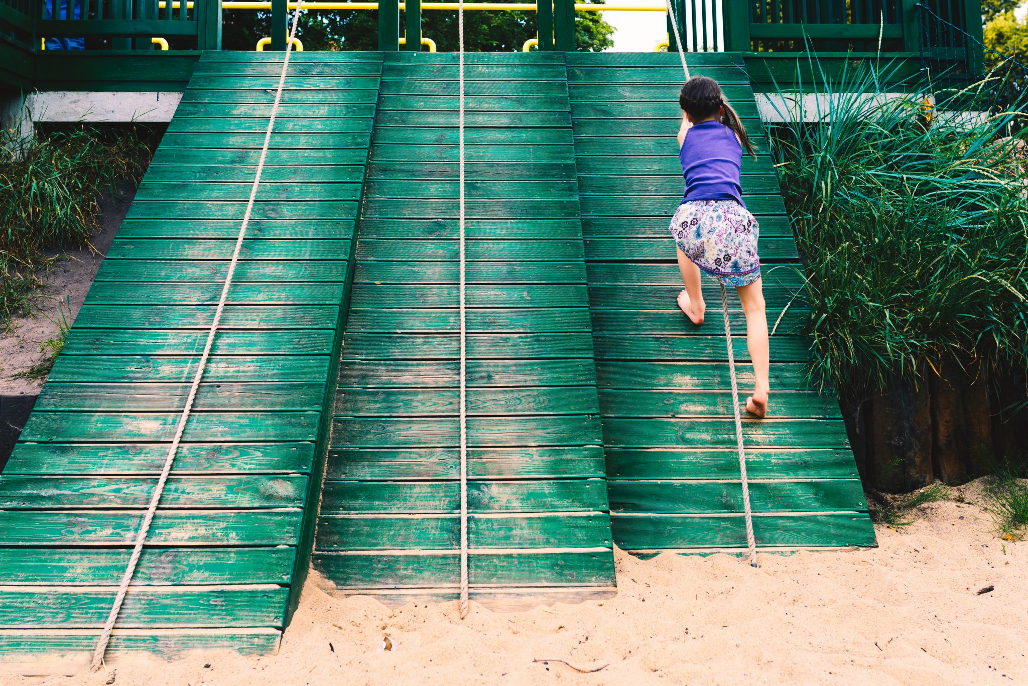 Little Girl Climbing A Wooden Wall Outdoor At Children Playground little-girl-climbing-a-wooden-wall-outdoor-at-children-playground
